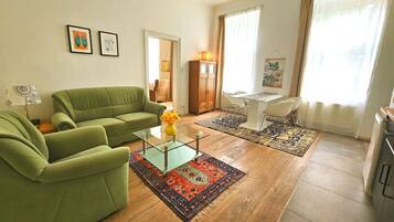 Uma sala de estar com um sofá verde, uma mesa de centro de vidro e um tapete estampado.