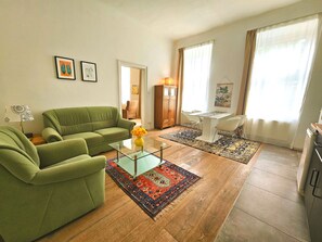 Uma sala de estar com um sofá verde, uma mesa de centro de vidro e um tapete estampado.