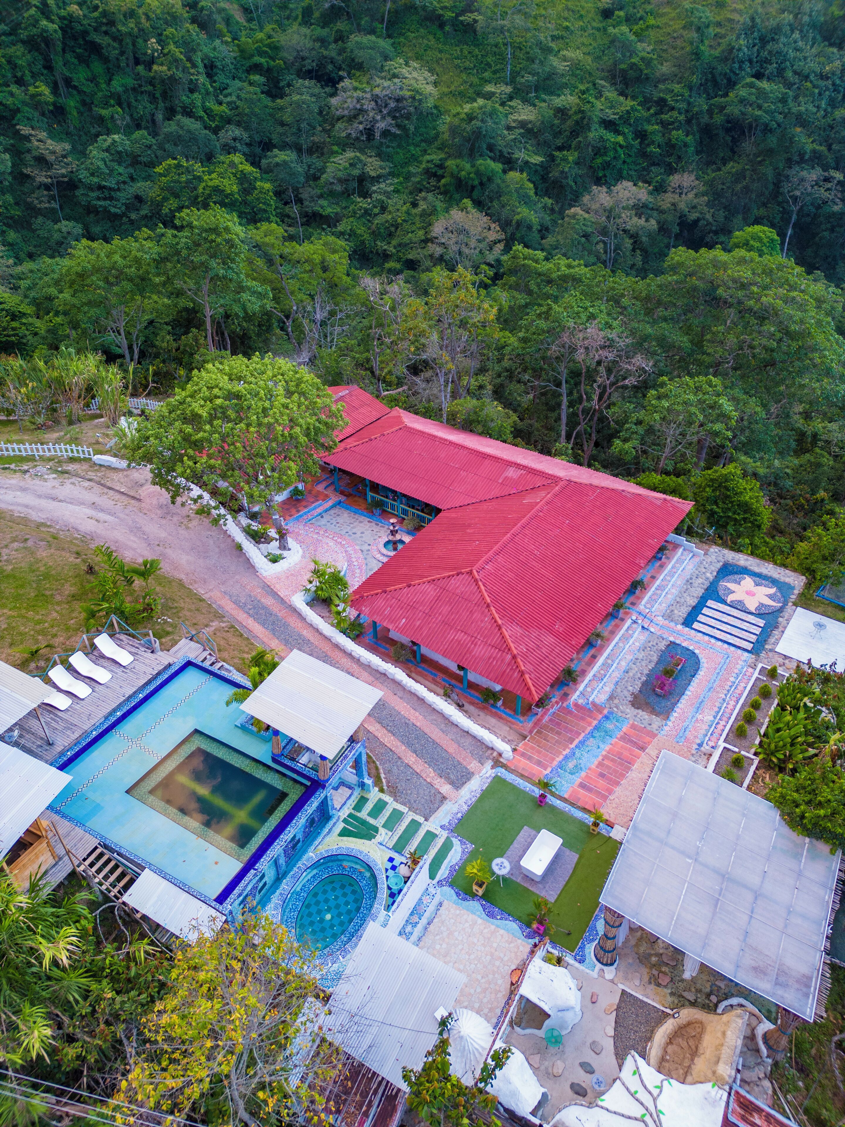 Vista aérea de um resort com piscina, um edifício de telhado vermelho e um jardim ajardinado.