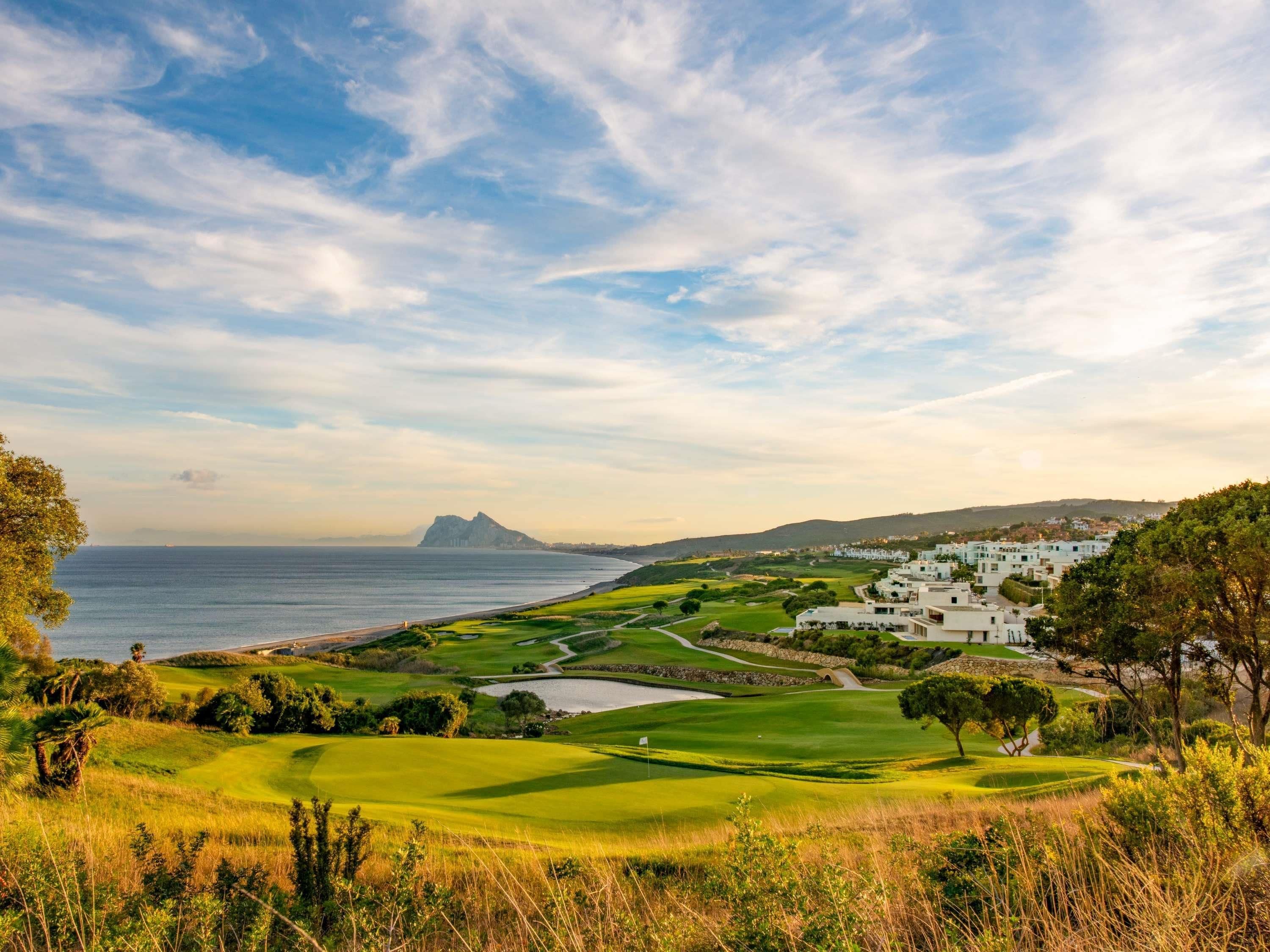 Um campo de golfe costeiro com vista para o mar e uma montanha ao longe.