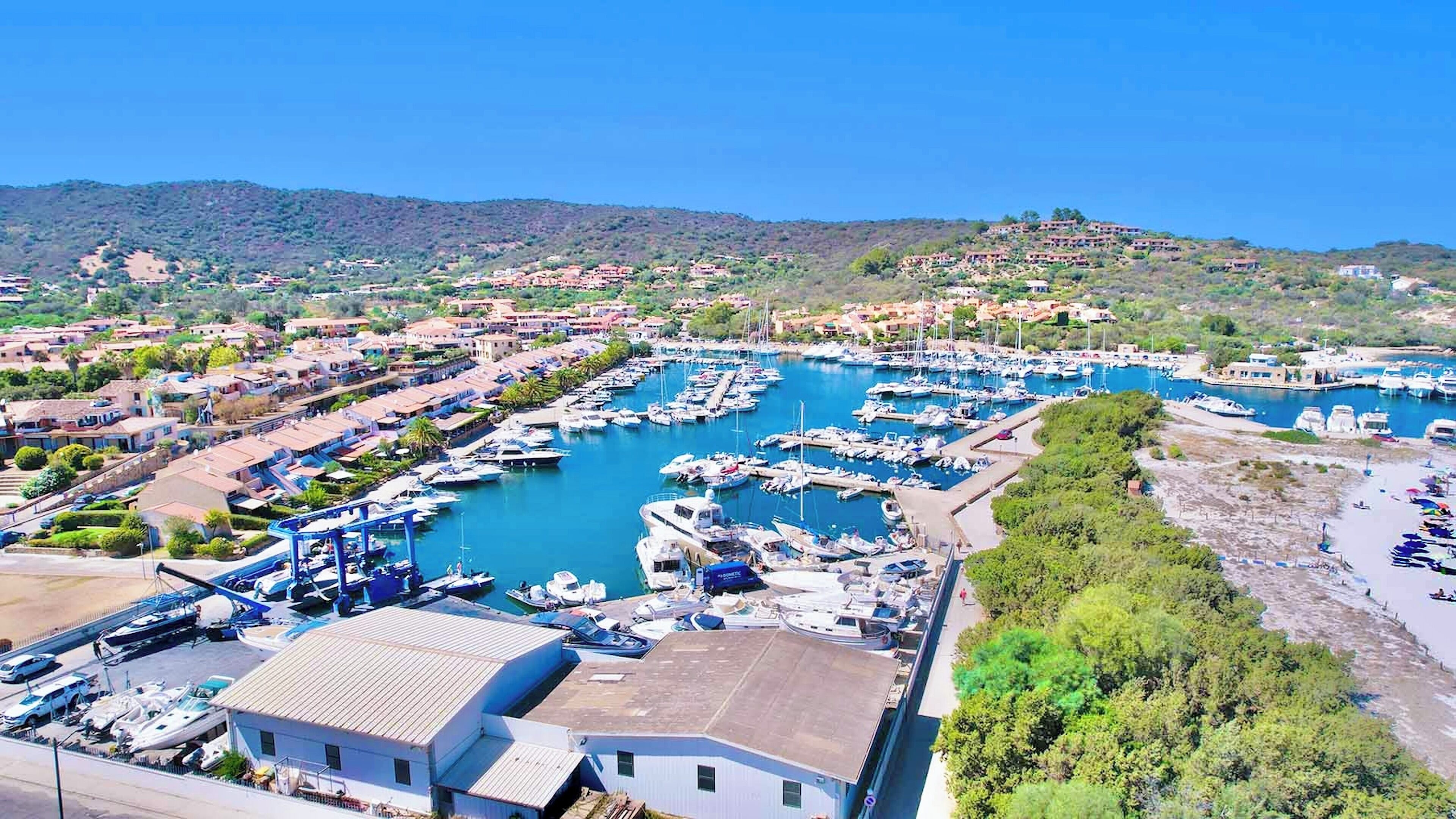 Uma marina com vários barcos atracados, rodeada por edifícios residenciais e vegetação.