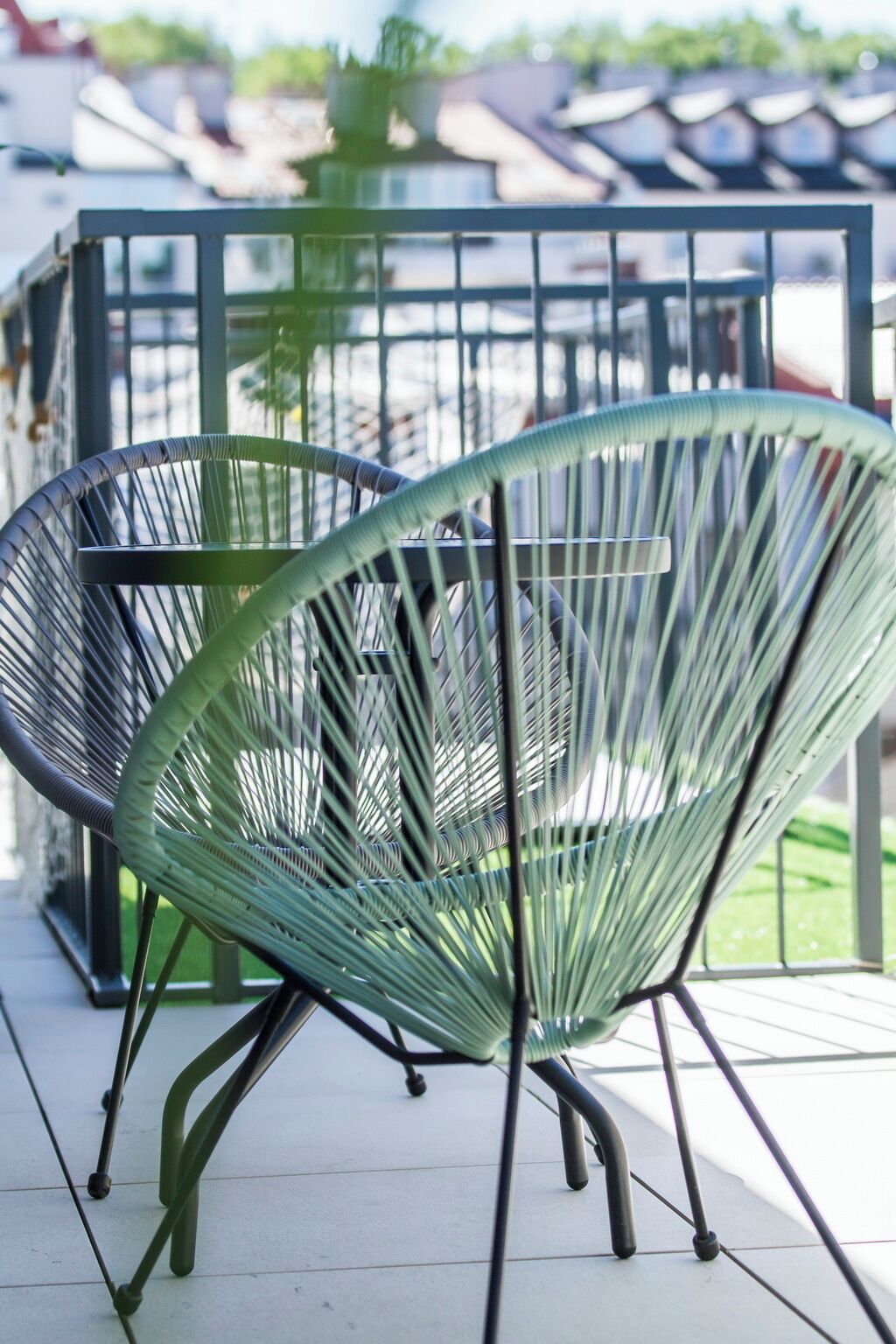 Duas cadeiras de estrutura verde em um pátio com guarda-corpo de metal e vista para casas ao fundo.