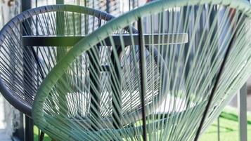 Duas cadeiras de estrutura verde em um pátio com guarda-corpo de metal e vista para casas ao fundo.