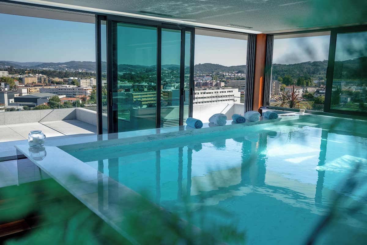 Piscina interior moderna com barreira de vidro, vista para a paisagem urbana e céu claro.