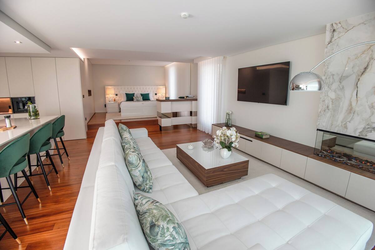 Uma sala de estar moderna com um sofá branco grande, uma mesa de centro e uma televisão na parede.