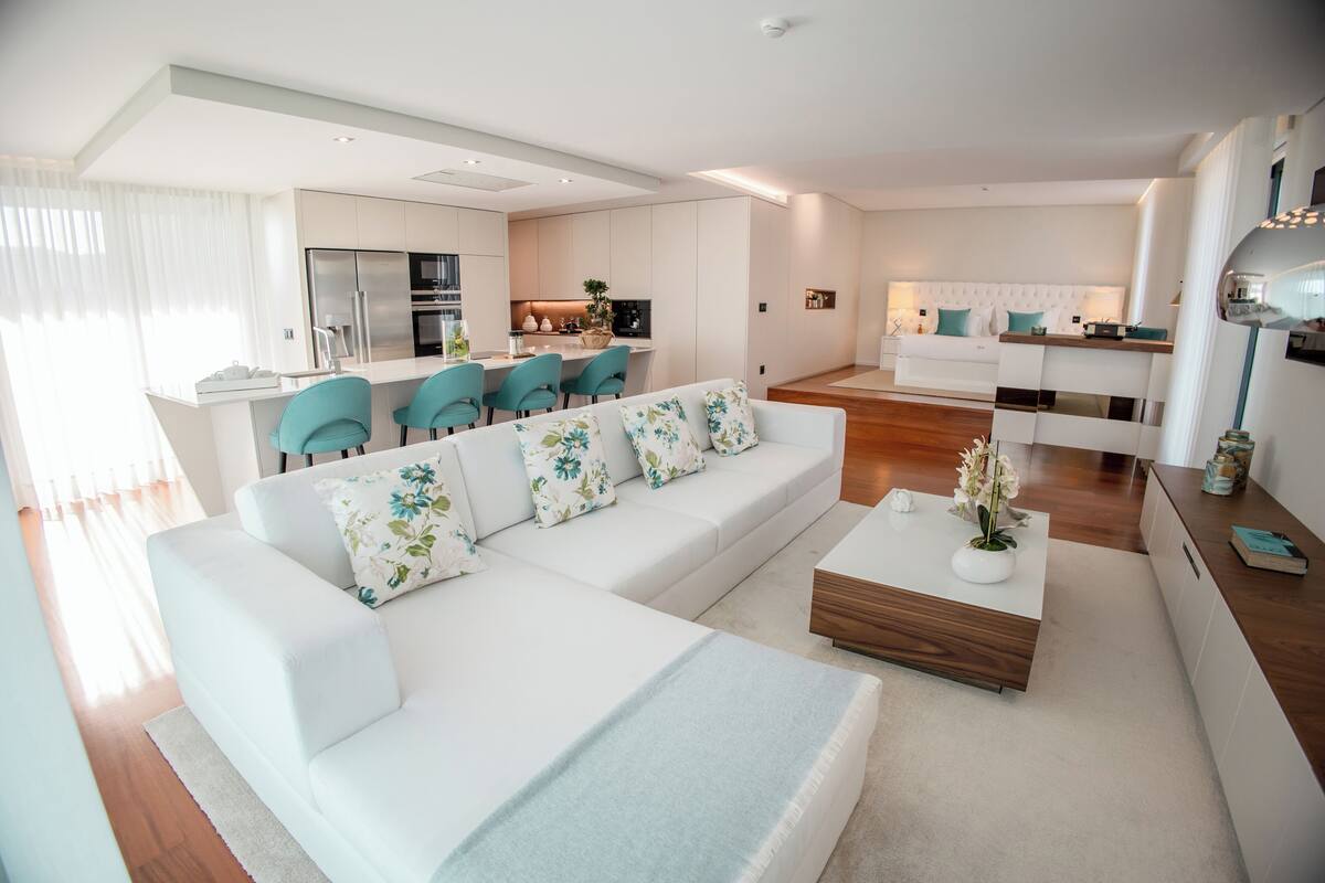 Uma sala de estar moderna com um sofá branco, cadeiras azul-turquesa e uma mesa de centro de madeira.