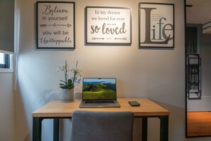 Uma mesa com um laptop, um smartphone e um vaso de planta. Há cartazes motivacionais na parede.
