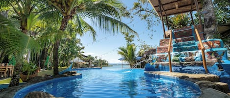 Resort tropical com piscina azul cristalina, palmeiras e estrutura de madeira com a placa 'Jacuzi'.