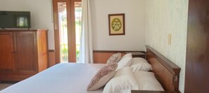 Um quarto com cama, cabeceira de madeira, televisão sobre um móvel e janela com cortinas.