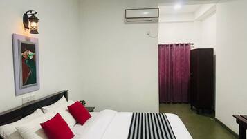 Quarto de hotel com cama, mesa de cabeceira, ar-condicionado fixado na parede, quadro emoldurado e porta com cortina.