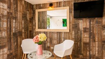 Quarto com paredes de madeira, mesa de vidro redonda com uma cadeira branca, um vaso rosa com flores e um espelho fixado acima da mesa.