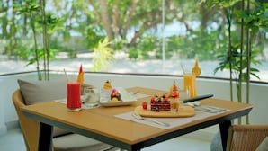 Uma mesa de jantar com sobremesa, bebidas e um prato de comida, com vista para uma paisagem tropical.