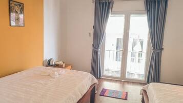Quarto com duas camas, uma luminária no teto, uma janela com cortinas e uma porta que dá para uma varanda.