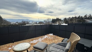 Um pátio externo com vista para montanhas, cerca preta e uma mesa com almofada.