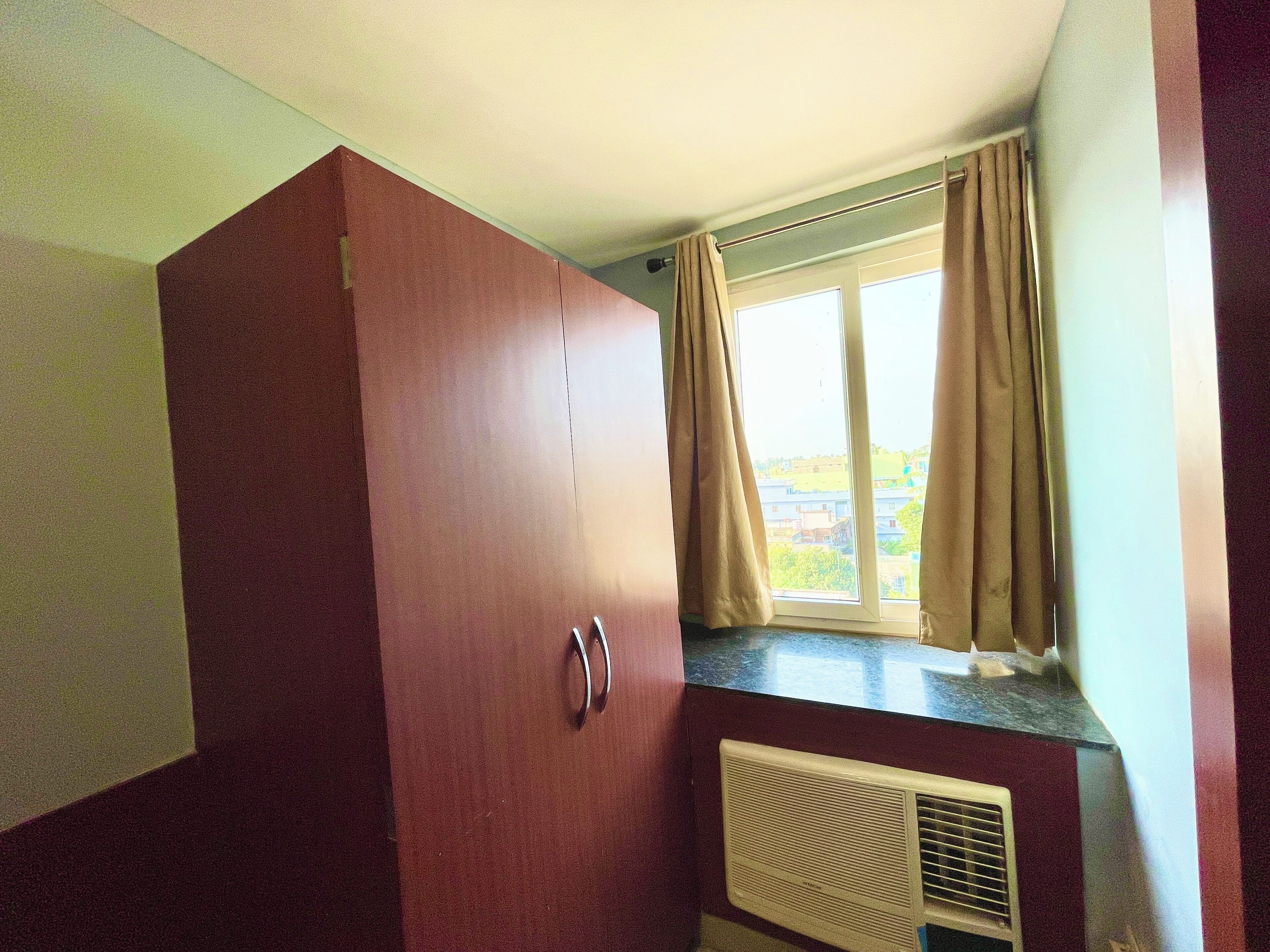 Quarto com guarda-roupa espaçoso, janela com cortinas e radiador.