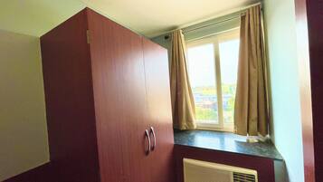 Quarto com guarda-roupa espaçoso, janela com cortinas e radiador.