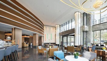 Um hall de hotel moderno com teto curvo, área de estar central e grandes janelas com vista para a cidade.