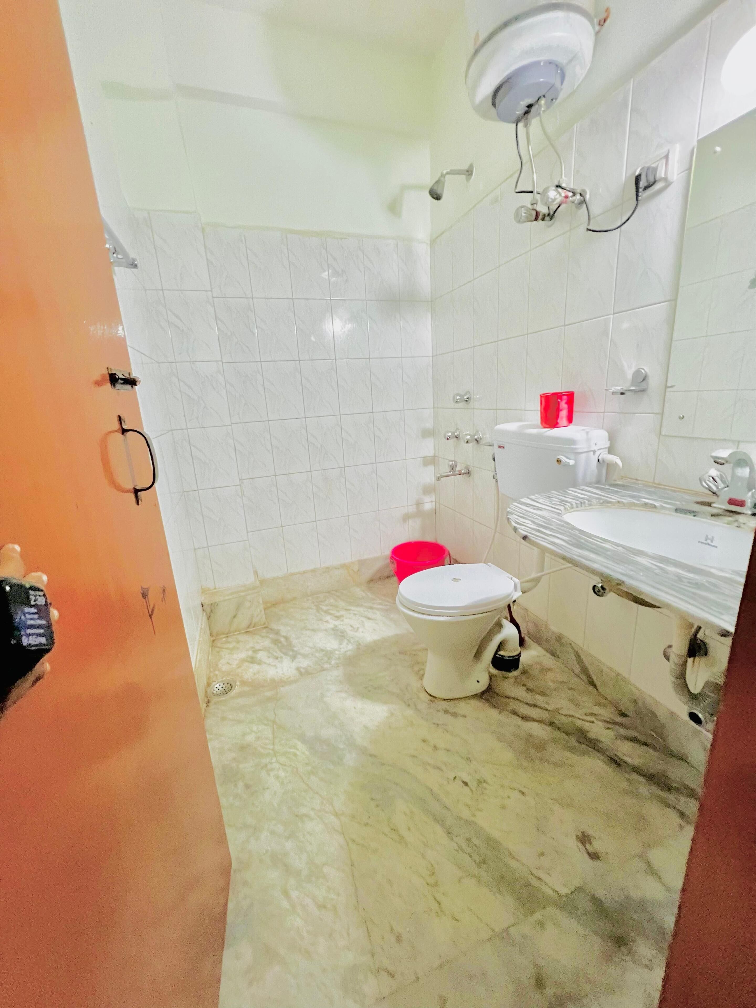 Casa de banho com paredes revestidas a azulejos brancos, sanita, lavatório com espelho e ventoinha no teto.