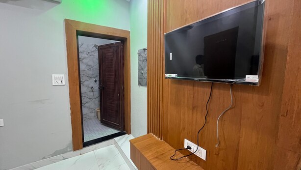 Quarto com porta de madeira, televisão na parede e chão revestido de azulejos.