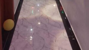 Um corredor com piso de mármore, paredes decoradas com balões amarelos e brancos, e uma área de recepção ao fundo.