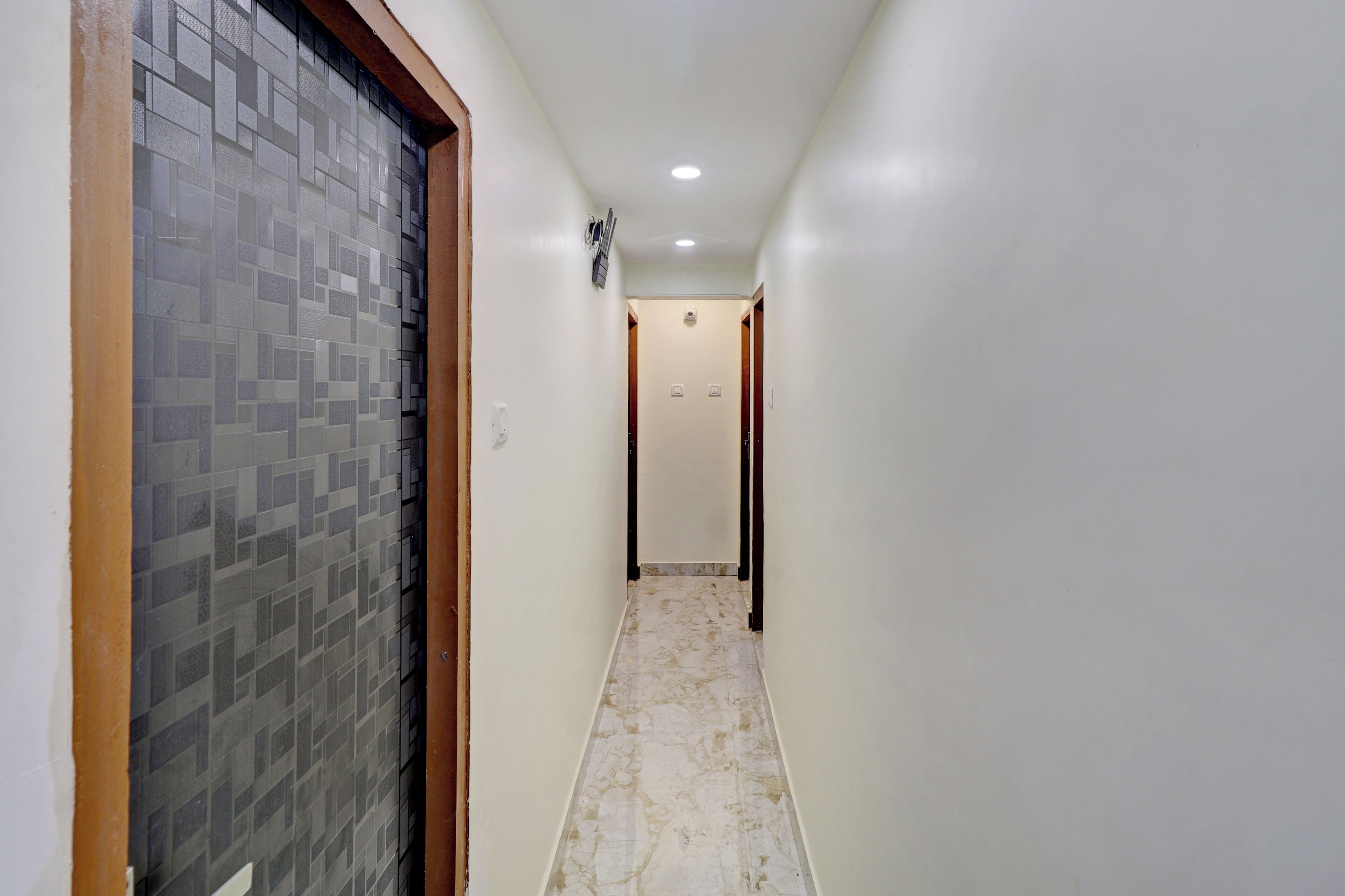 Um corredor estreito, com uma parede revestida de azulejos à esquerda e uma parede lisa à direita.