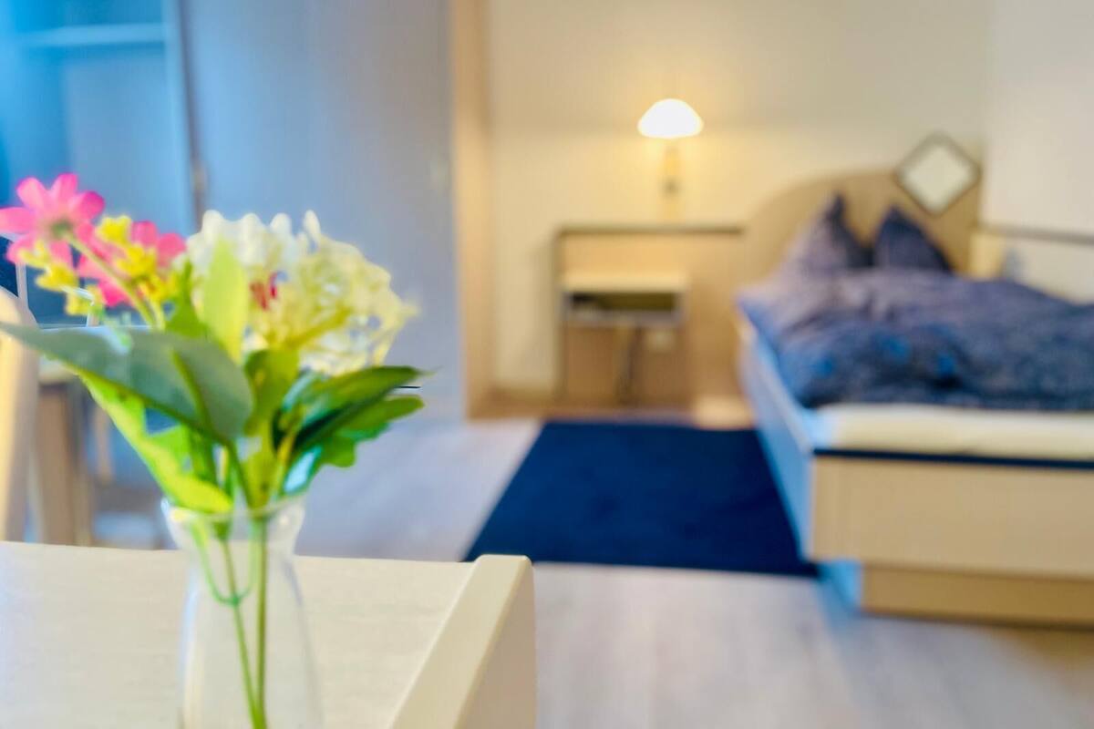 Um quarto com cama, mesa de cabeceira, abajur e um vaso com flores.