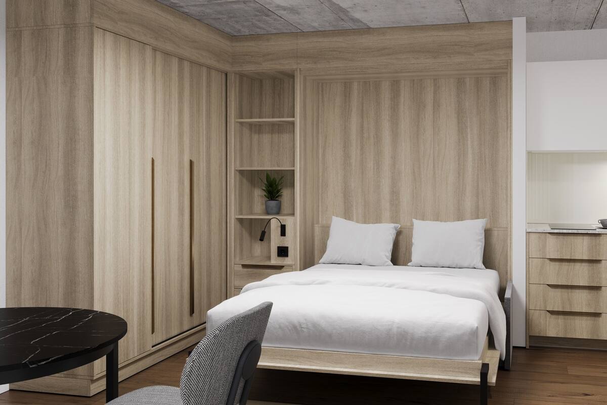 Quarto moderno com cama, mesas de cabeceira, escrivaninha e uma cozinha compacta.