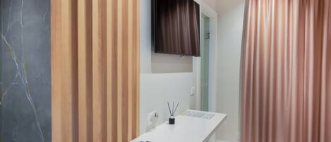 Uma casa de banho moderna com uma toucador branco, uma televisão montada e chão de madeira.