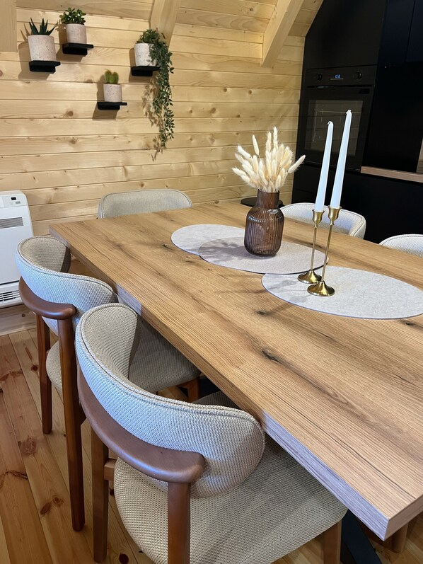 Uma mesa de jantar de madeira com cadeiras, um vaso com plumas de capim-do-campo e um castiçal.