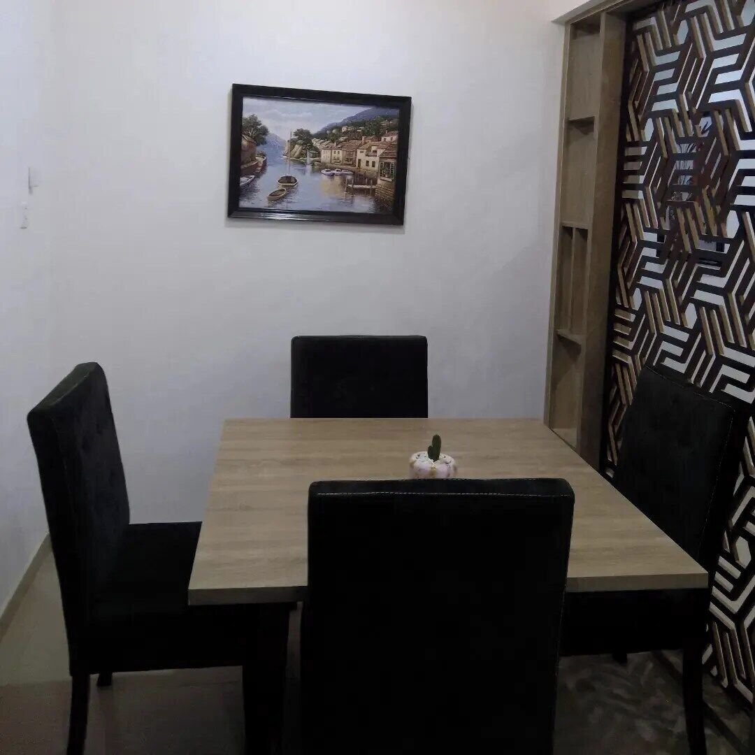 Uma sala de jantar com uma mesa de madeira, quatro cadeiras pretas, um quadro emoldurado de uma paisagem fluvial e um separador com padrão.