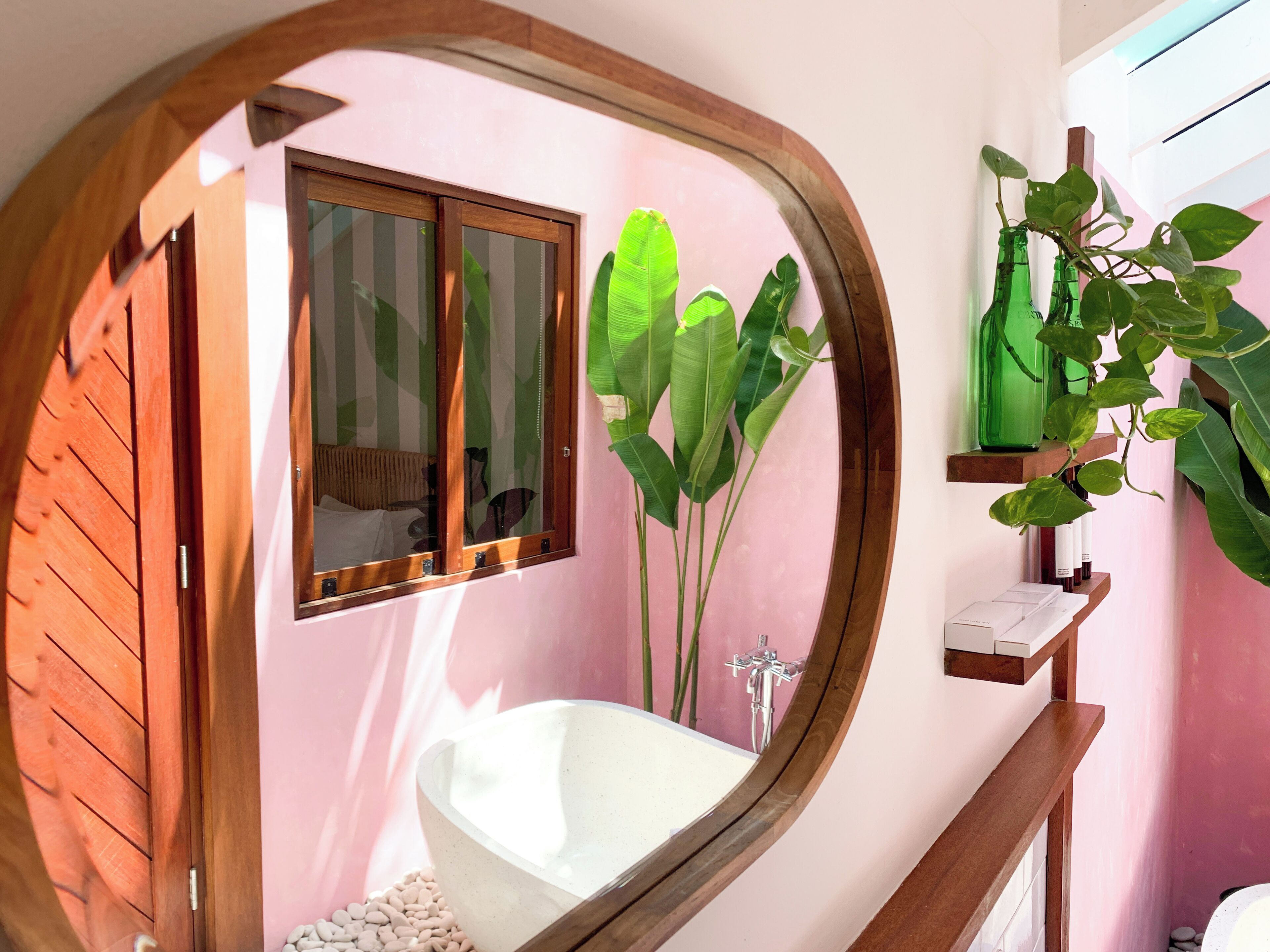 Um banheiro com uma banheira separada, uma porta de madeira e um espelho refletindo uma janela e uma planta.