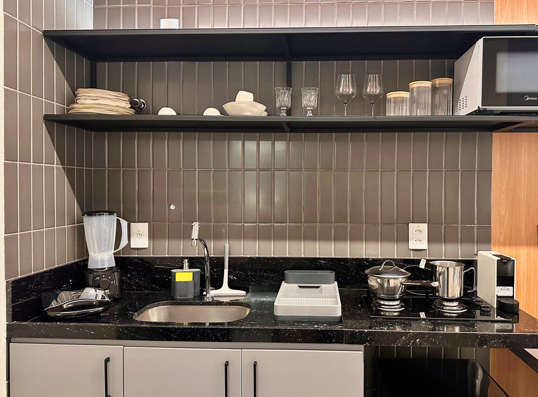 Cozinha moderna com bancada preta, cuba de aço inoxidável e micro-ondas sobre a bancada.