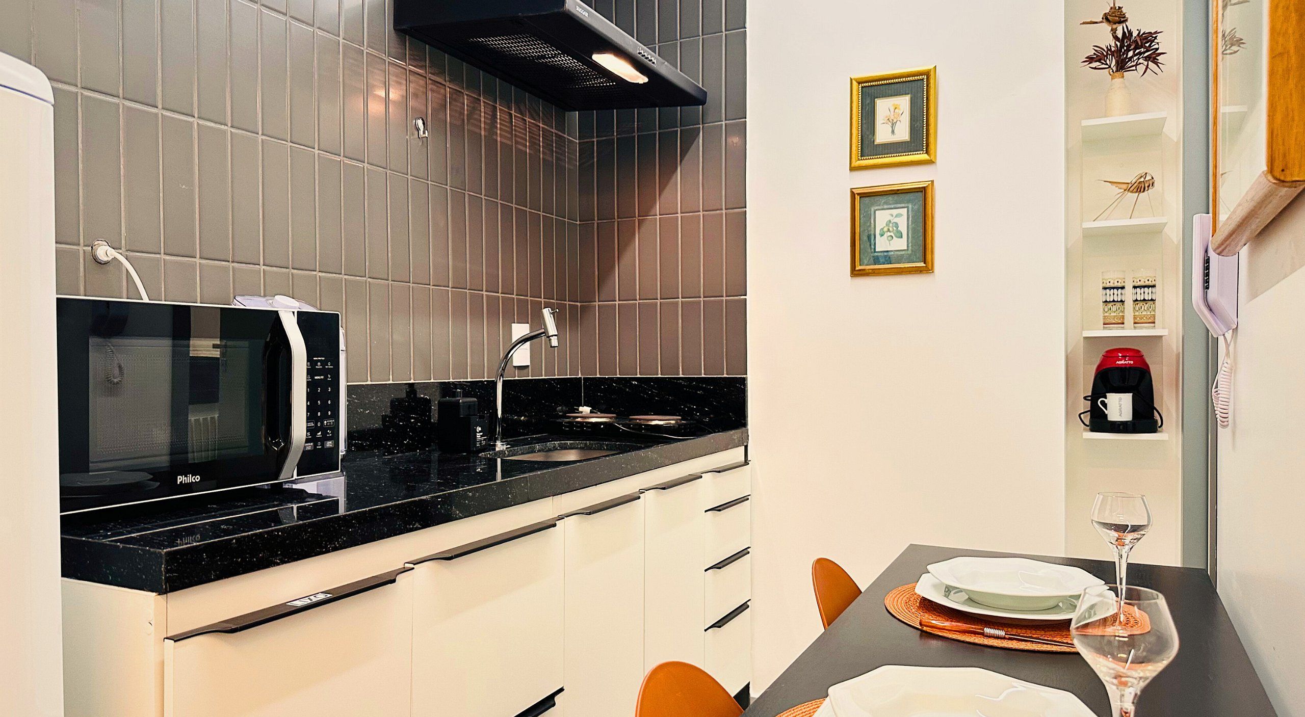 Uma cozinha moderna com bancada preta, armários brancos e micro-ondas embutido.