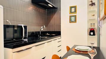 Uma cozinha moderna com bancada preta, armários brancos e micro-ondas embutido.