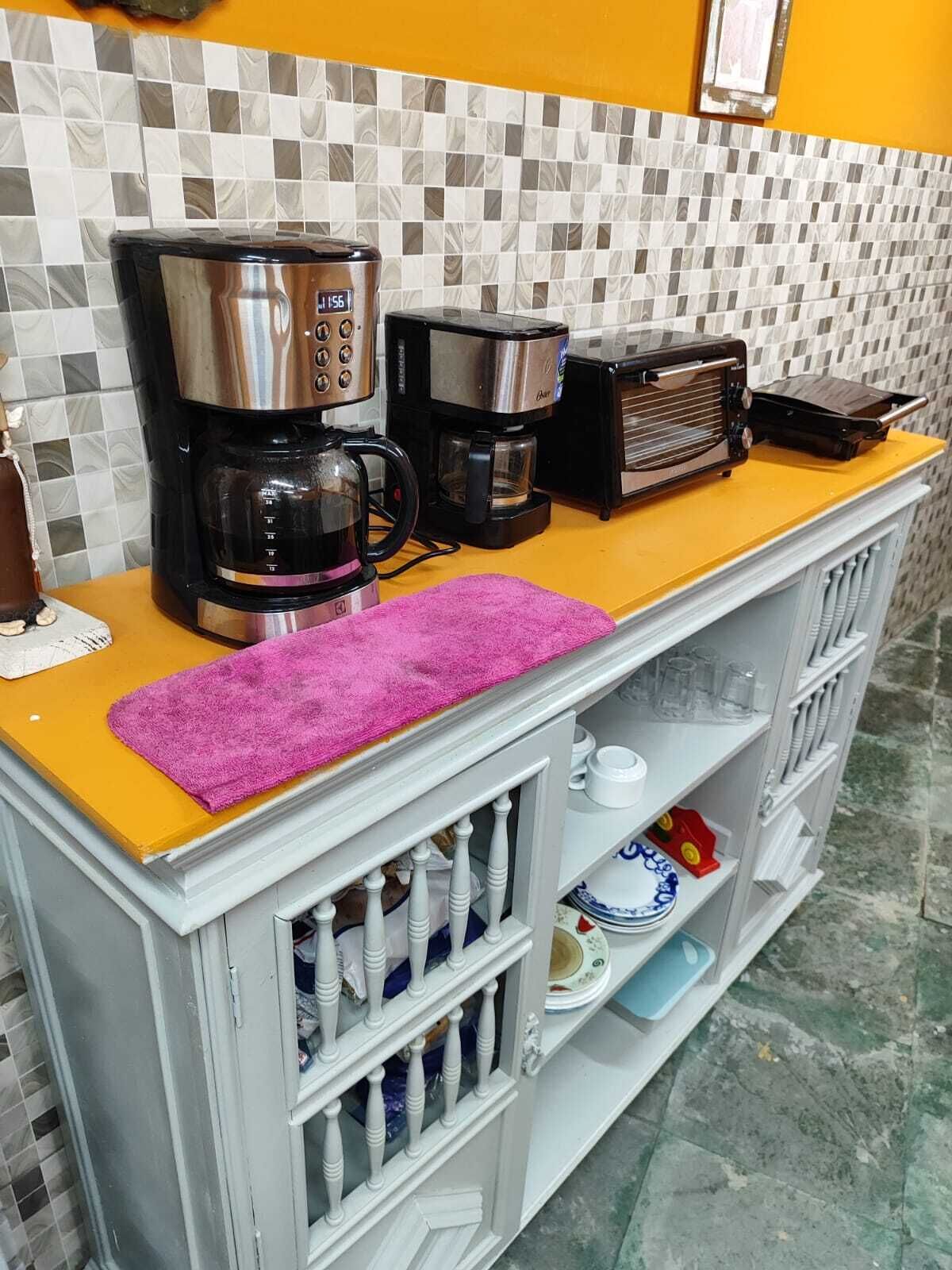 Cozinha com cafeteira, torradeira e micro-ondas em bancada amarela.