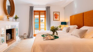 Quarto de hotel com lareira, cama com roupa de cama branca, mesa de cabeceira com abajur e janela com cortinas.