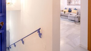 Escadaria com degraus brancos e corrimão azul que leva a uma sala de estar com sofá e almofadas.