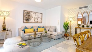 Uma sala de estar moderna com sofá, mesa de centro, banquinho e área de jantar com cadeiras.