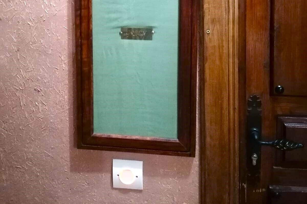 Um quadro emoldurado numa parede com textura, uma porta com puxador de latão e um interruptor de luz.