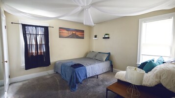 Quarto com cama, janela, quadro e ventoinha no teto.