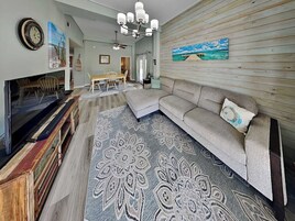 Uma sala de estar com sofá, televisão, parede de madeira e tapete estampado.
