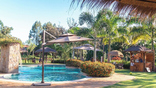 Uma área de piscina com guarda-sóis, um pequeno quiosque e vegetação exuberante.