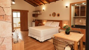 Quarto com teto de madeira, uma cama, mesa de cabeceira, cômoda, janela e área de jantar com mesa e cadeiras.