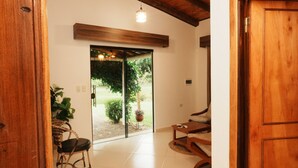Quarto com porta de madeira, porta de vidro deslizante que dá para área externa com plantas em vasos e vista para vegetação.