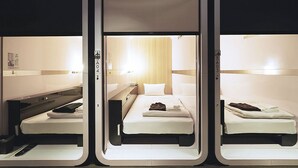 Quarto de hotel com três camas dispostas em linha, cada uma com mesa de cabeceira e abajur.