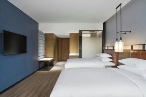 Quarto de hotel moderno com duas camas, televisão de tela plana, piso de madeira e um espelho grande.
