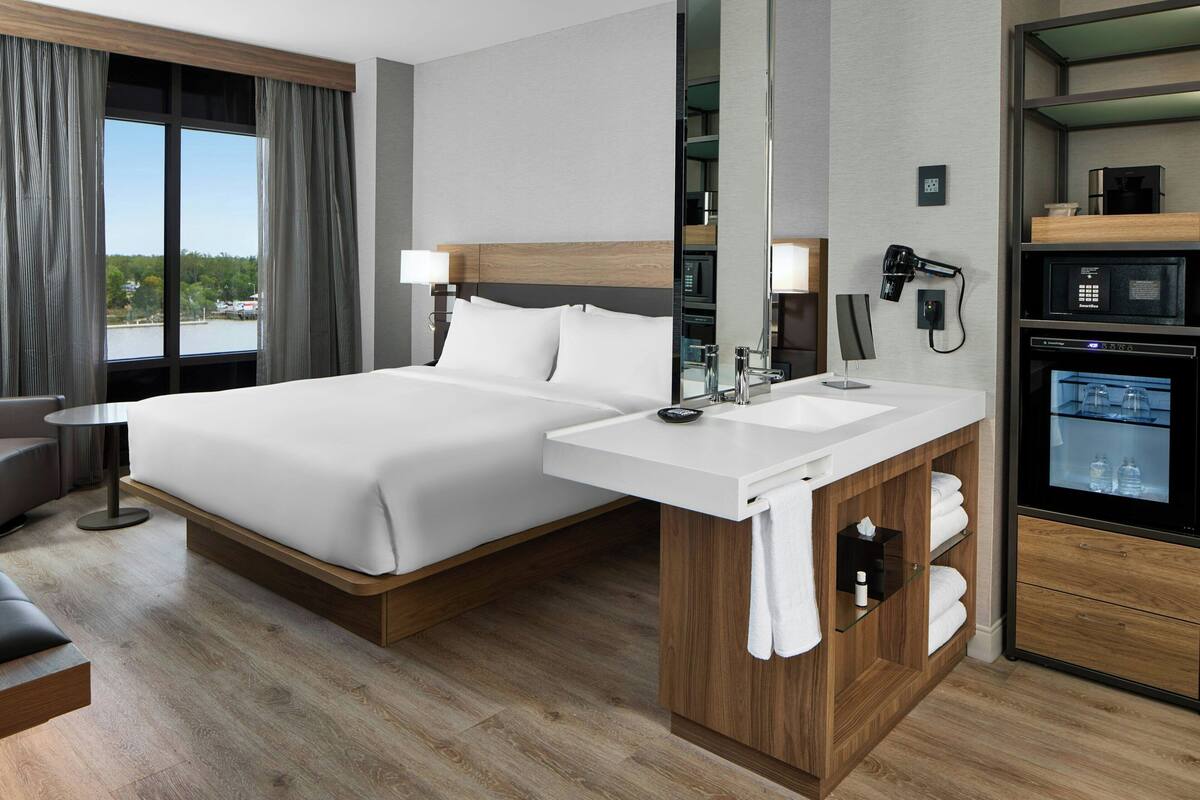 Quarto de hotel com uma cama grande, uma mesa de cabeceira, um espelho, forno embutido e vista para o exterior.