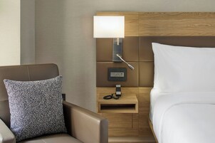 Quarto de hotel com cama, mesa de cabeceira, luminária, tomada e telefone.