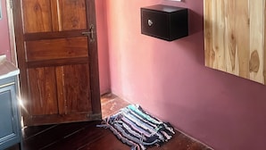 Um quarto com porta de madeira, um ar condicionado, uma caixa de armazenamento preta e um suporte de madeira com cabides.