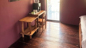 Um quarto com escrivaninha de madeira, uma cadeira, uma cama, um quadro e uma porta de correr com vidro.